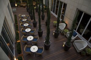 Uma área de pátio ao ar livre com várias mesas e cadeiras, rodeada por vasos de plantas e um deck de madeira.