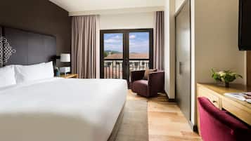 Quarto de hotel com uma cama grande, uma mesa de trabalho com cadeira, televisão e varanda com cortinas.