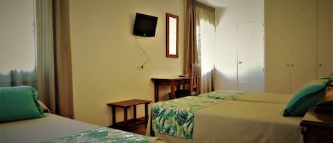 Quarto de hotel com duas camas, uma escrivaninha, uma cadeira, uma televisão e um guarda-roupa.