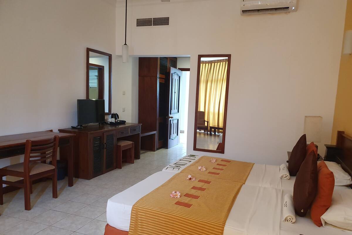 Quarto de hotel com cama, escrivaninha, cadeira, televisão e ar condicionado.