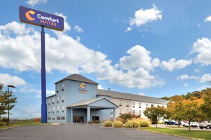 Um hotel Comfort Suites com um amplo estacionamento, uma placa visível e um edifício de vários andares com telhado plano.