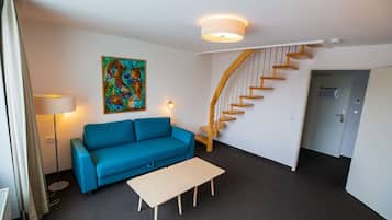 Sala de estar com um sofá azul, uma mesa pequena, escada de madeira e um quadro na parede.