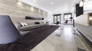 Uma sala de estar moderna com um sofá cinzento, um tapete escuro e uma parede de destaque em madeira.