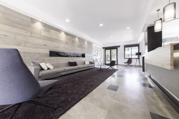Uma sala de estar moderna com um sofá cinzento, um tapete escuro e uma parede de destaque em madeira.