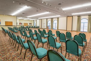 Uma sala de conferências com fileiras de cadeiras azul-turquesa, um tapete estampado e amplas janelas com cortinas.