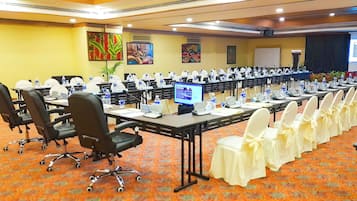 Uma sala de conferências com mesas, cadeiras dispostas em fileiras e uma tela grande na frente.