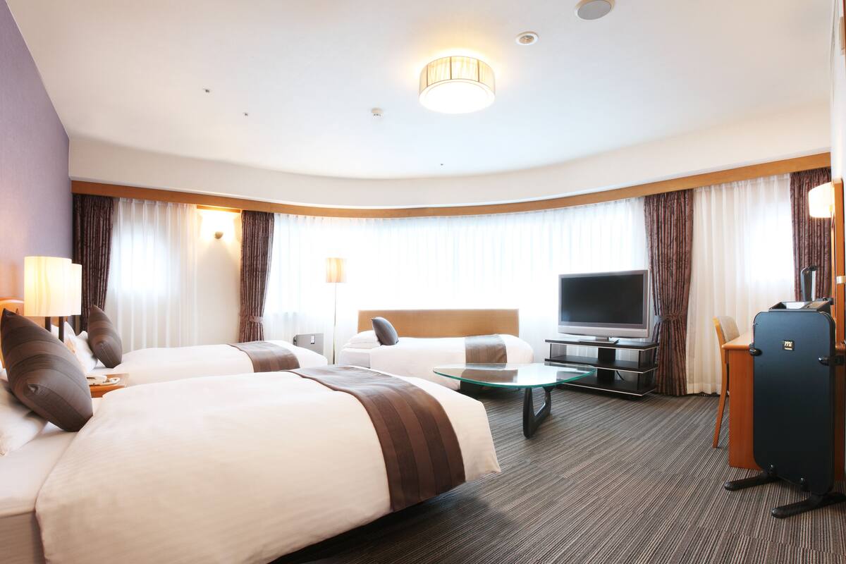 Quarto de hotel com duas camas, uma televisão, uma escrivaninha e uma cadeira.