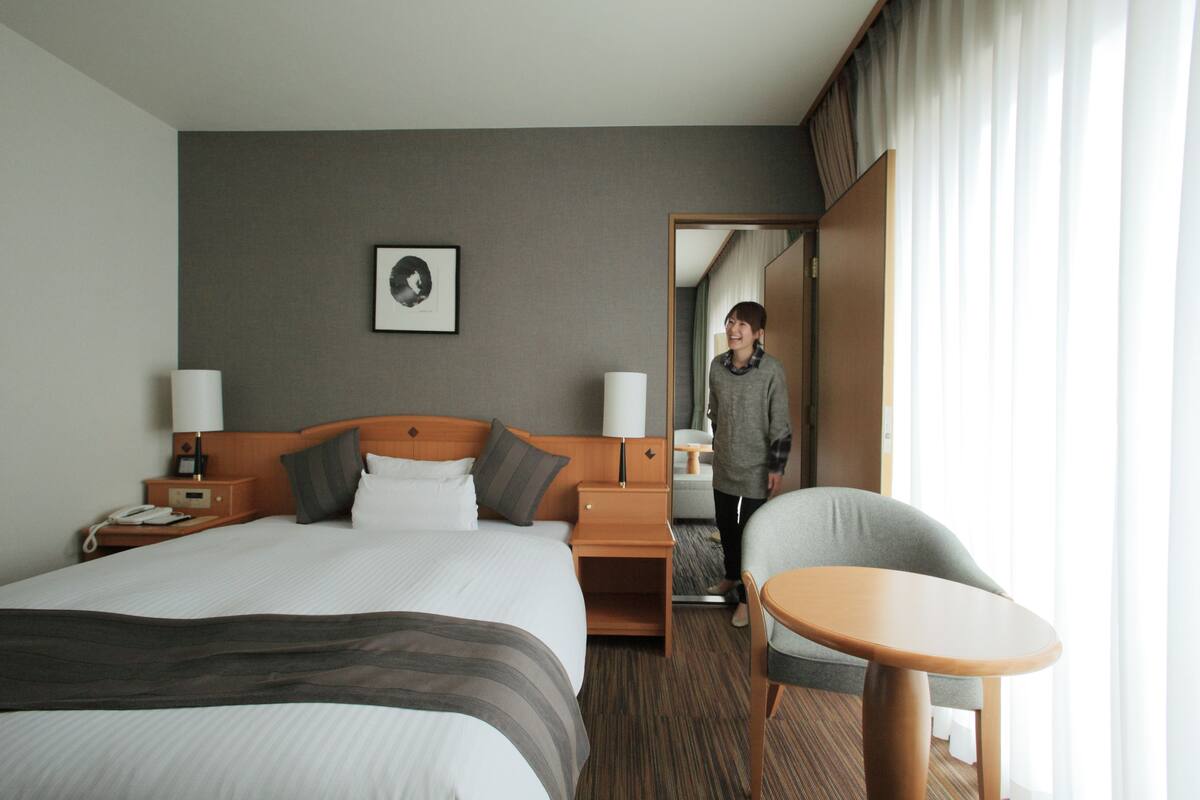 Quarto de hotel com uma cama grande, mesas de cabeceira, uma cadeira e uma pequena mesa.
