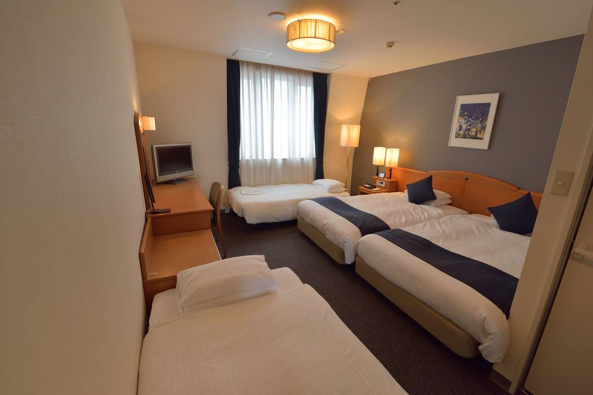 Quarto de hotel com duas camas, uma escrivaninha com computador, uma luminária e um quadro na parede.