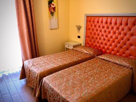 Quarto de hotel com duas camas, cabeceira vermelha, mesa de cabeceira e um quadro na parede.
