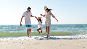Uma família caminhando em uma praia de areia, com o oceano ao fundo.