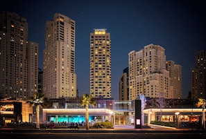 Um hotel com vários edifícios altos ao fundo, entrada bem iluminada e áreas de estar ao ar livre.
