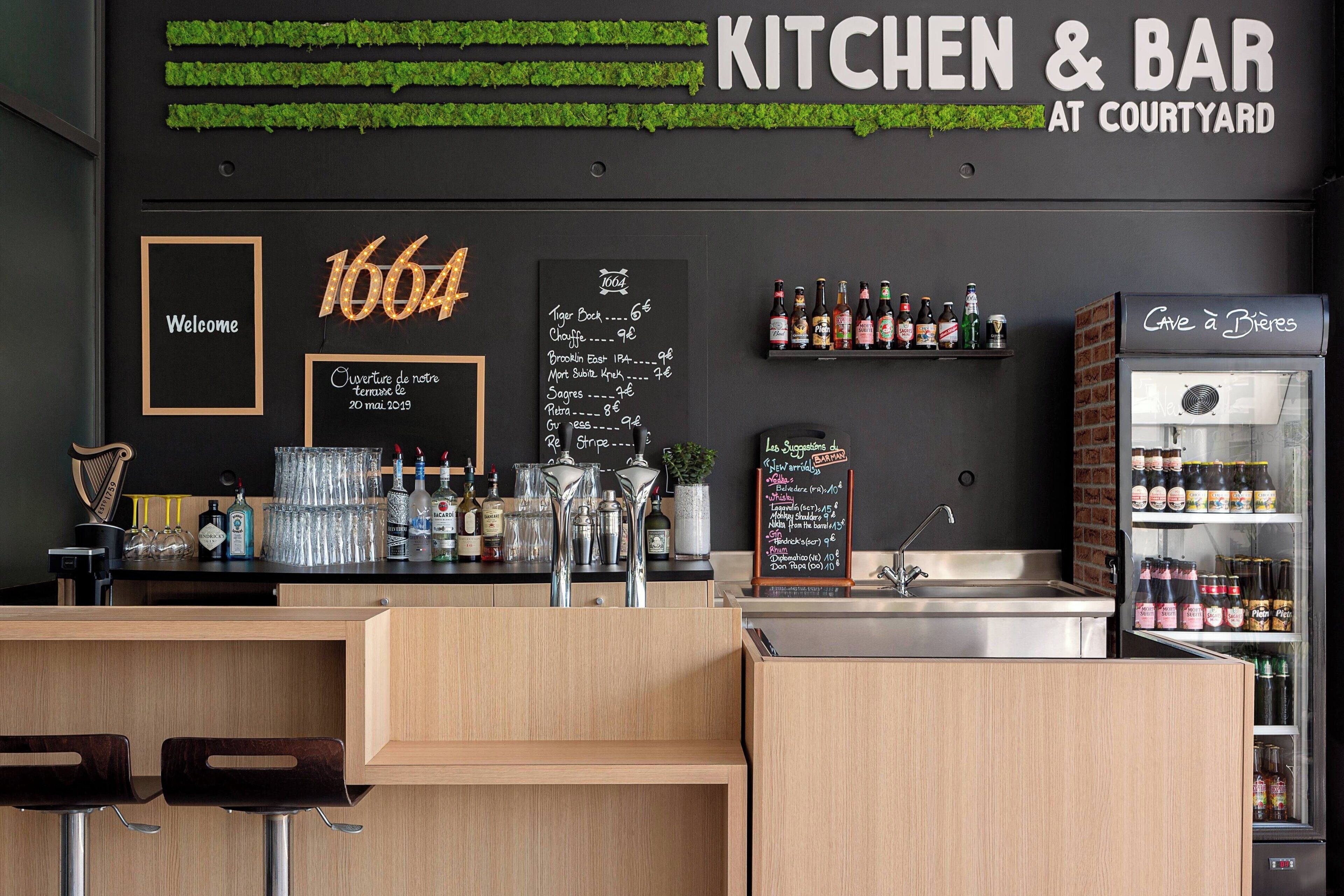 Cozinha e bar com cardápio em lousa, prateleiras com garrafas e uma geladeira.