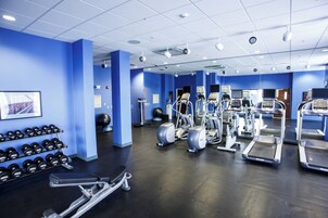 Academia com equipamentos de ginástica, halteres e esteira.