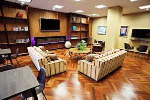 Um hall de hotel com área de estar, televisão e estante de livros.