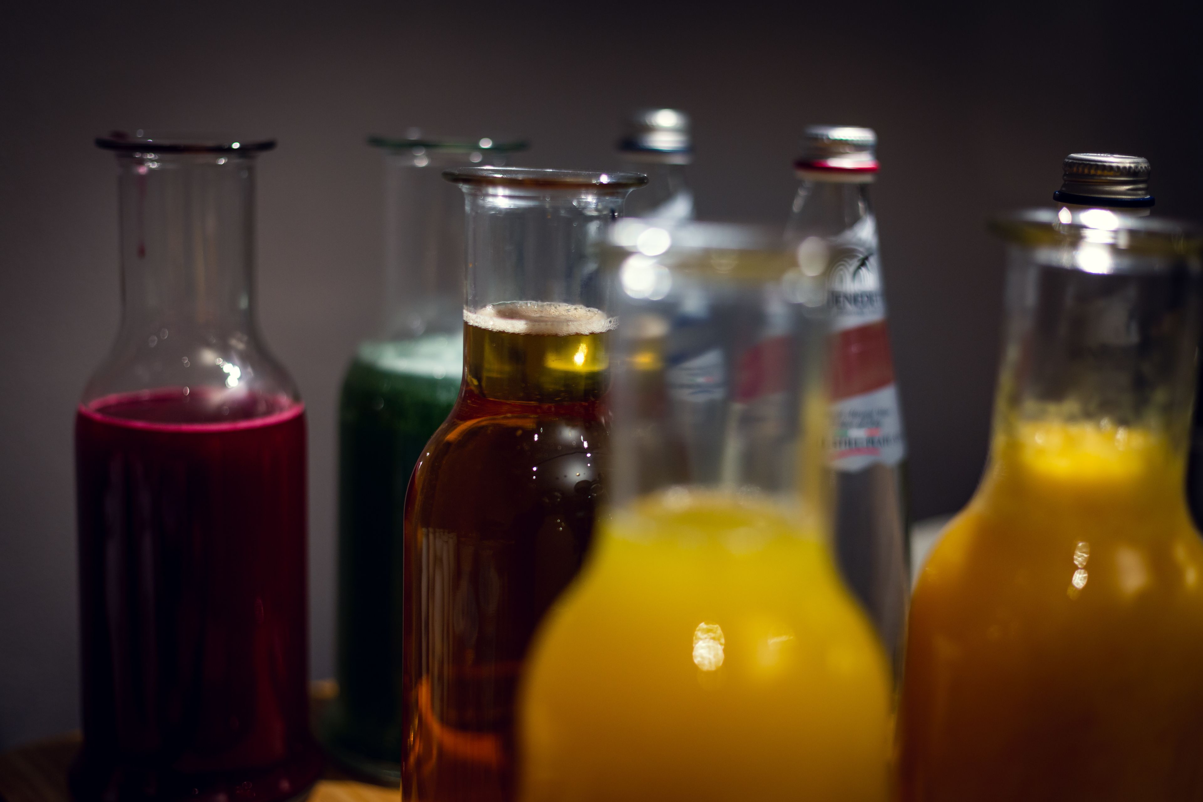 Uma fileira de garrafas de vidro transparente com líquidos de cores diferentes, possivelmente para uso científico ou culinário.