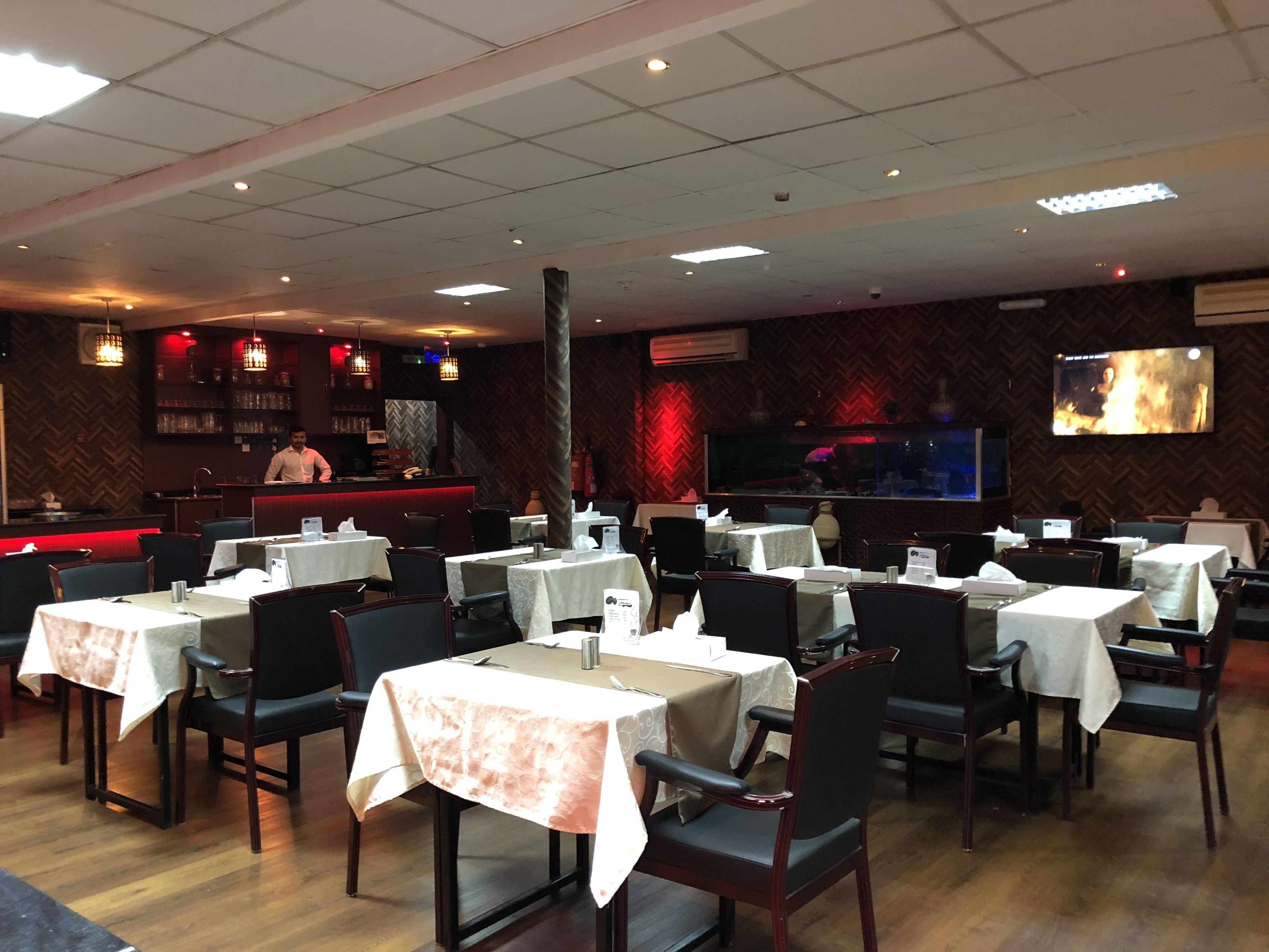 Um restaurante com várias mesas, cadeiras, um espaço de bar e uma televisão exibindo uma chama.