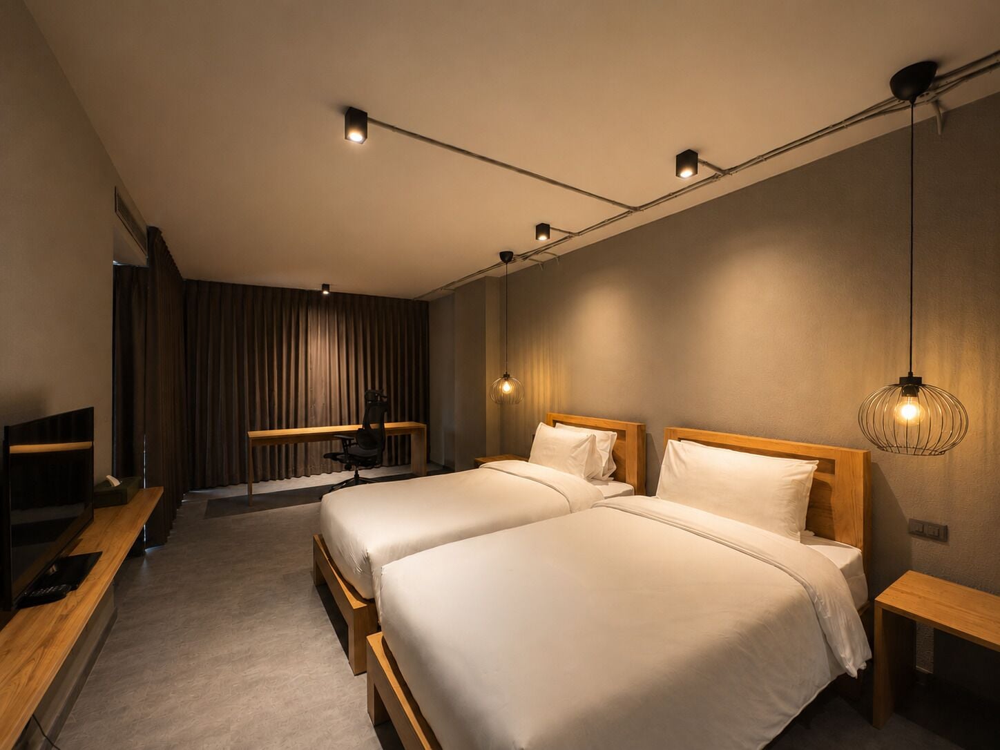 Quarto de hotel moderno com duas camas, uma mesa e uma televisão.
