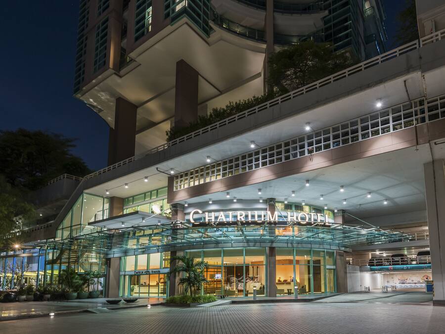 Um hotel moderno com fachada de vidro, área de estar ao ar livre e uma placa chamativa.
