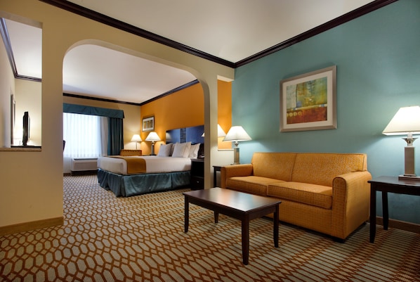 Quarto de hotel com cama, sofá, mesa de centro e um quadro na parede.