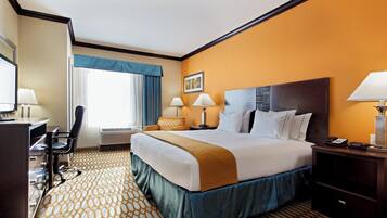 Quarto de hotel com cama, escrivaninha, cadeira e janela com cortinas.