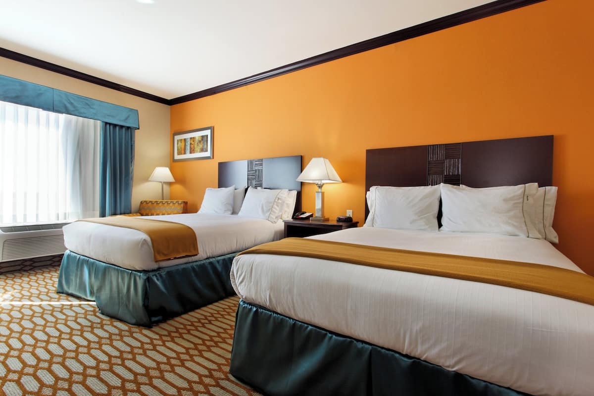 Quarto de hotel com duas camas, uma janela grande com cortinas azuis, um quadro na parede e um chão estampado.
