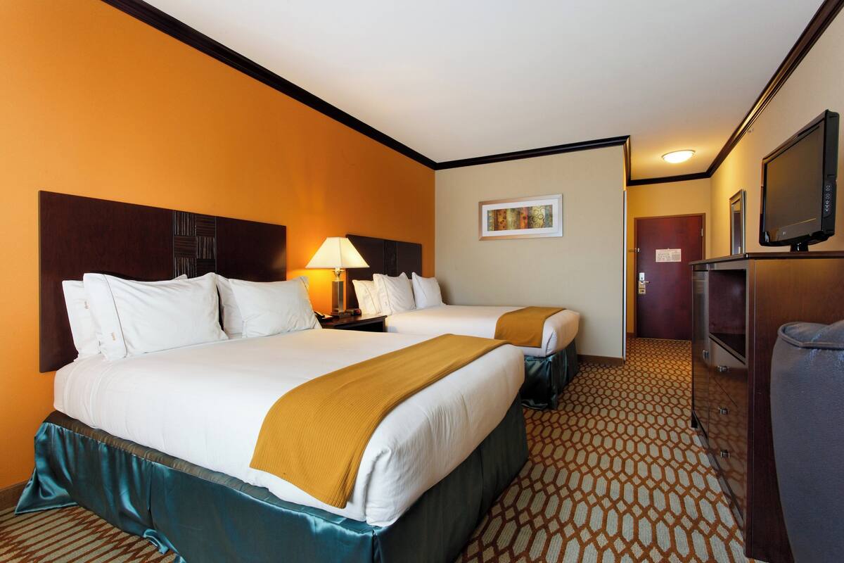 Quarto de hotel com duas camas, televisão e escrivaninha com luminária.