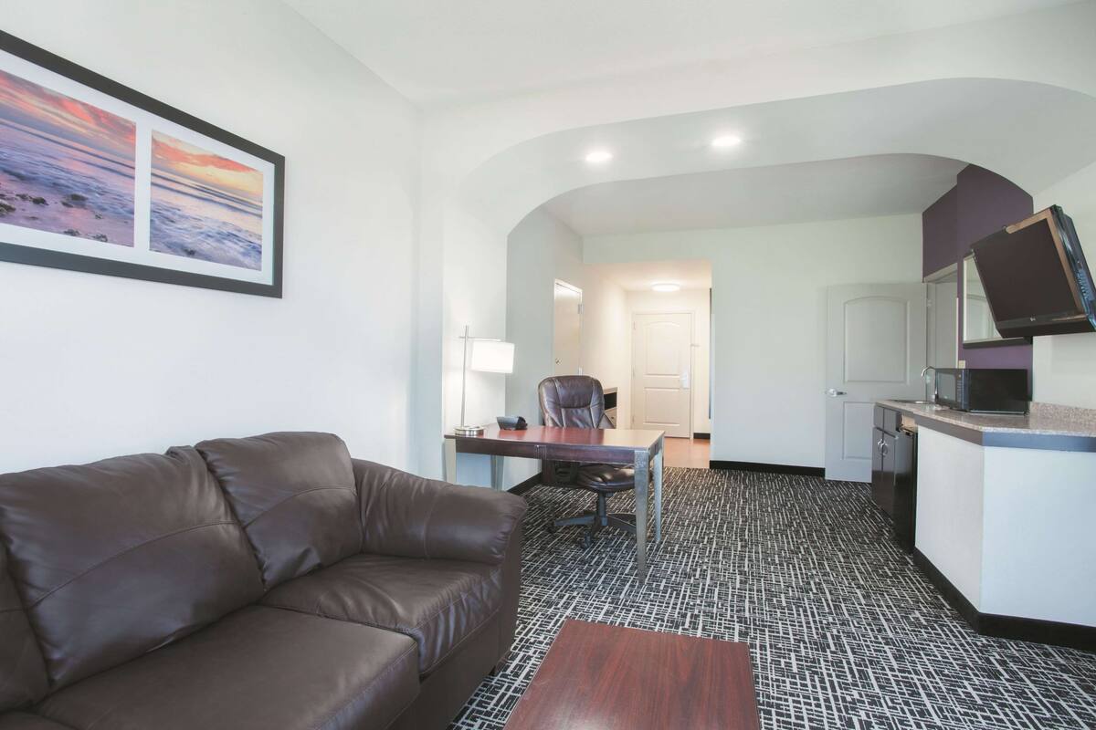Quarto de hotel moderno com sofá de couro, mesa de jantar, área de cozinha e um quadro na parede.