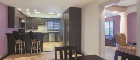 Uma cozinha moderna com armários escuros, uma sala de jantar com uma mesa e cadeiras de madeira escura, e vista para a sala de jantar.