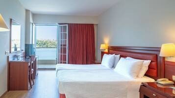 Quarto de hotel com cama, luminárias laterais, escrivaninha com telefone e vista para o exterior.