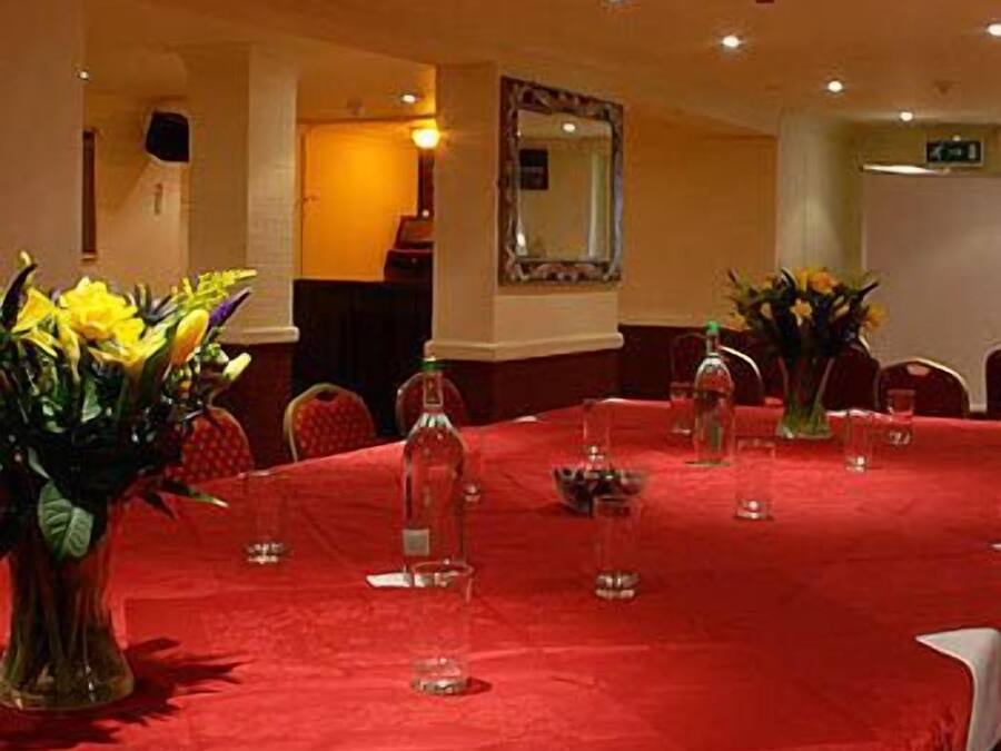Uma sala de conferência com toalha vermelha, vasos com flores e um espelho na parede.