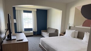 Quarto de hotel com cama, escrivaninha, cadeira, televisão e janela com cortinas.
