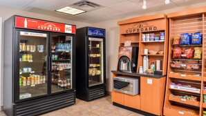 Espaço de café da manhã com serviço próprio, dispensers de bebidas refrigeradas, máquina de café e prateleiras com lanches e itens para o café da manhã.