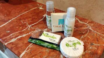Artigos de higiene pessoal, incluindo uma barra de sabonete, shampoo, loção corporal e outra barra de sabonete, sobre uma bancada de mármore.