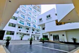 Um edifício moderno com vários andares, grandes janelas e um pátio central com plantas em vasos.
