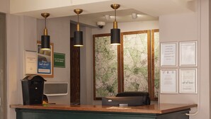 Bancada de recepção com painel verde, luminárias pendentes no teto, certificados emoldurados na parede e uma janela grande com vista para árvores.