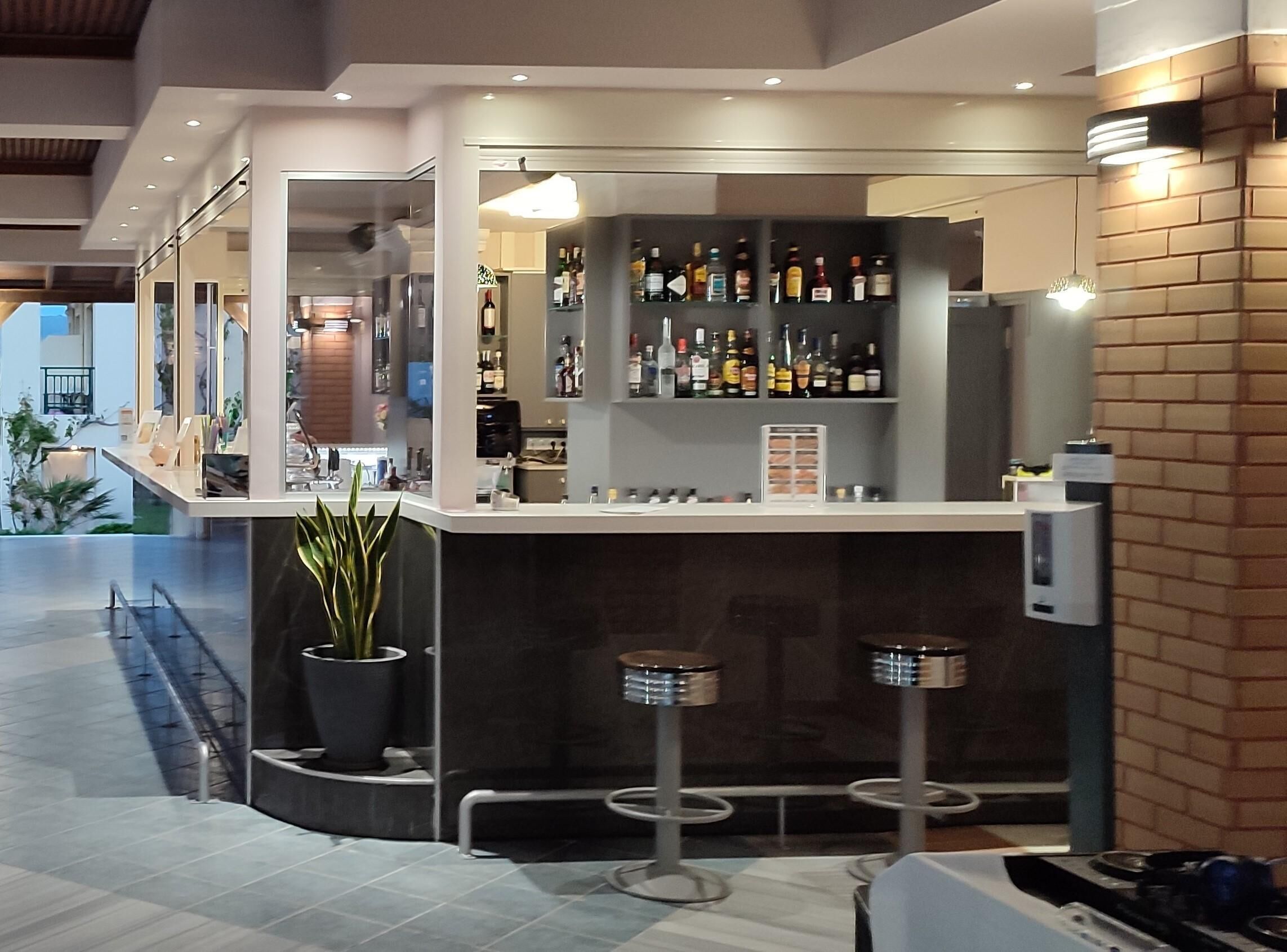 Uma área de bar moderna com balcão, banquetas e diversos tipos de garrafas nas prateleiras.