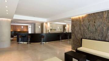 Um lobby moderno com balcão de recepção, área de estar e uma parede de pedra decorativa.