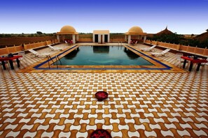 Uma área de piscina com um padrão geométrico de azulejos, espreguiçadeiras e uma piscina central.