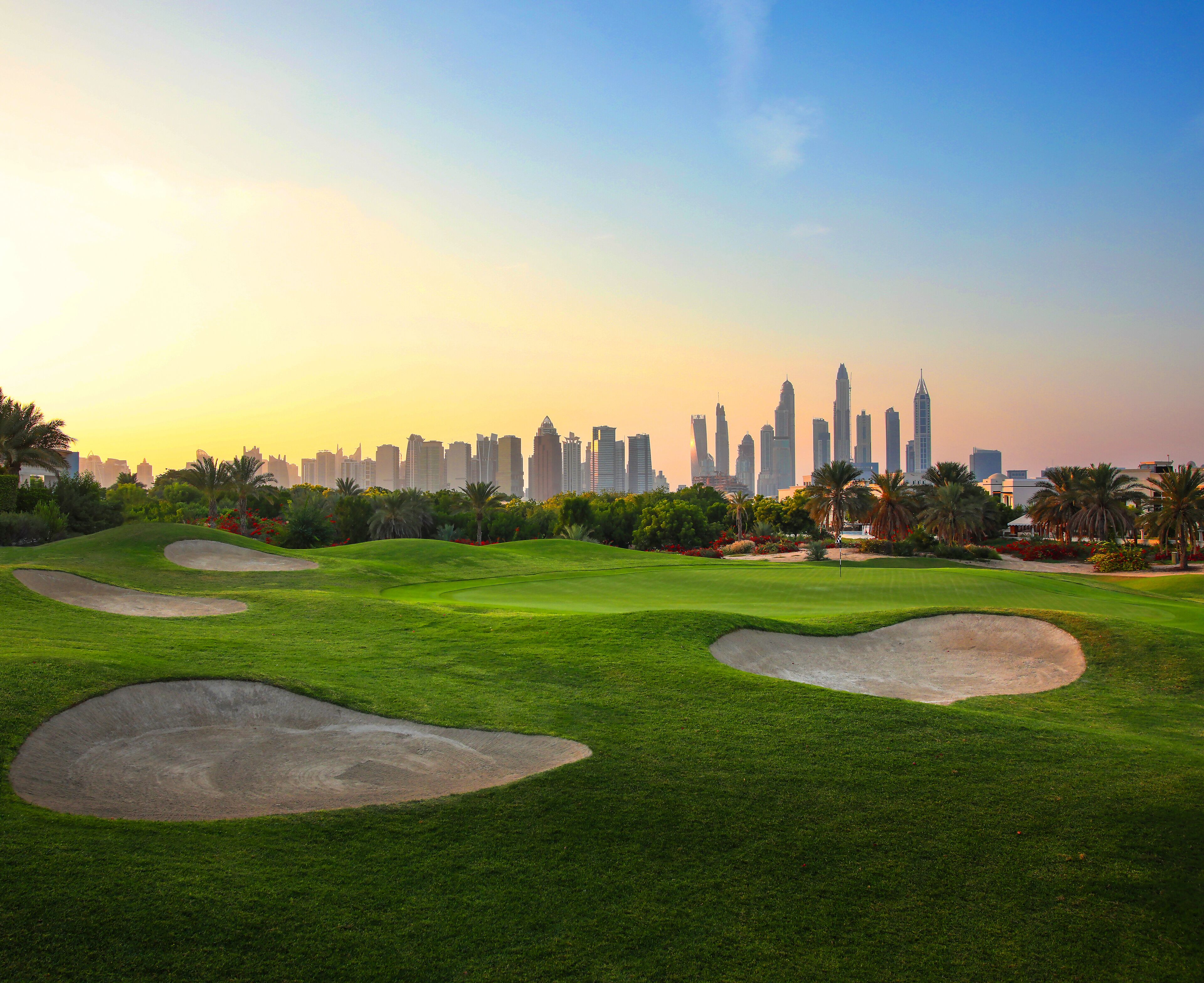 Um campo de golfe com bunkers de areia e o horizonte urbano ao fundo.