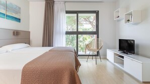 Quarto de hotel com duas camas, uma TV em um console branco, uma cadeira e uma janela com vista para árvores.