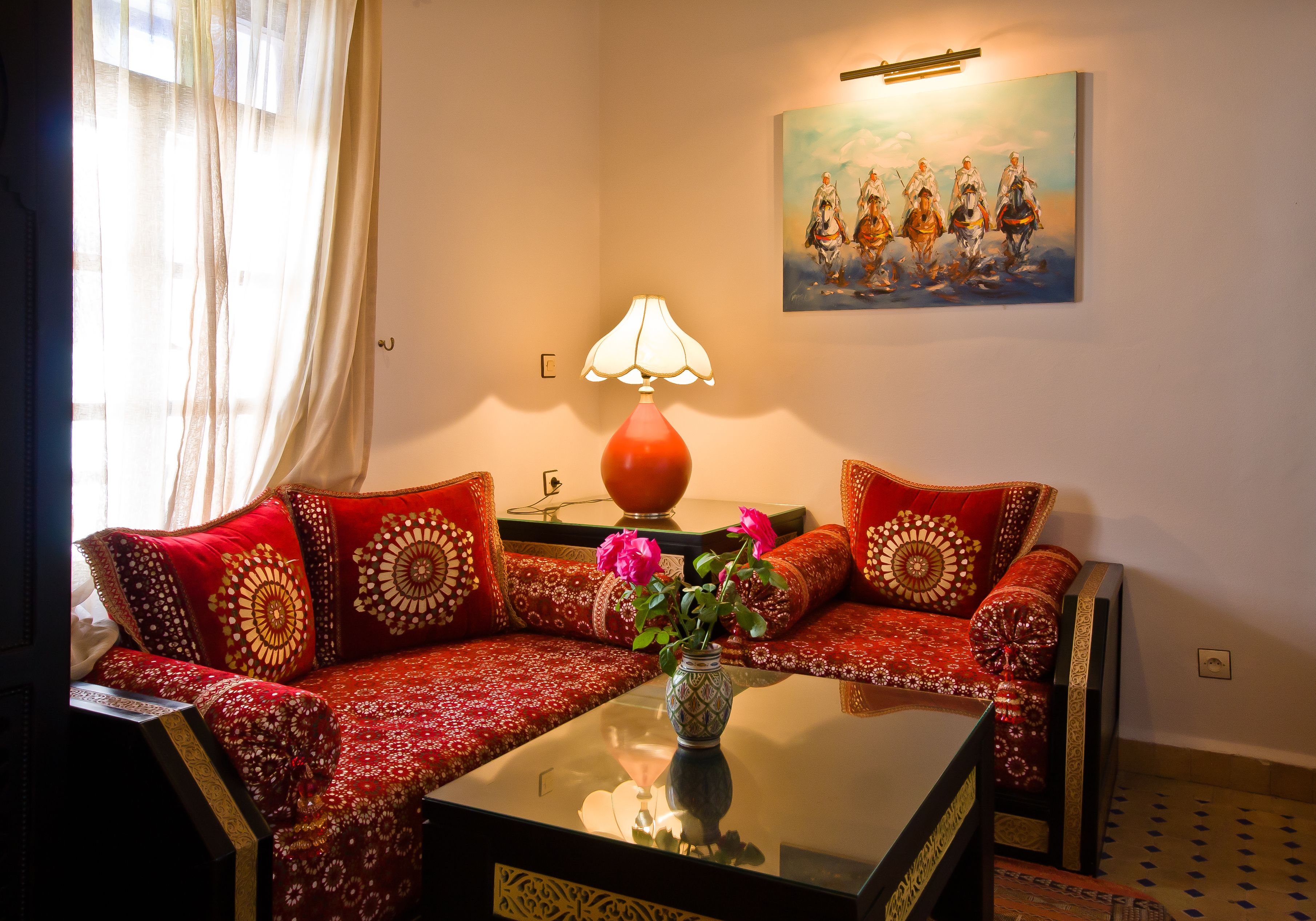 Uma sala de estar com sofá, mesa de centro, vaso com flores, luminária e quadro na parede.