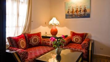 Uma sala de estar com sofá, mesa de centro, vaso com flores, luminária e quadro na parede.