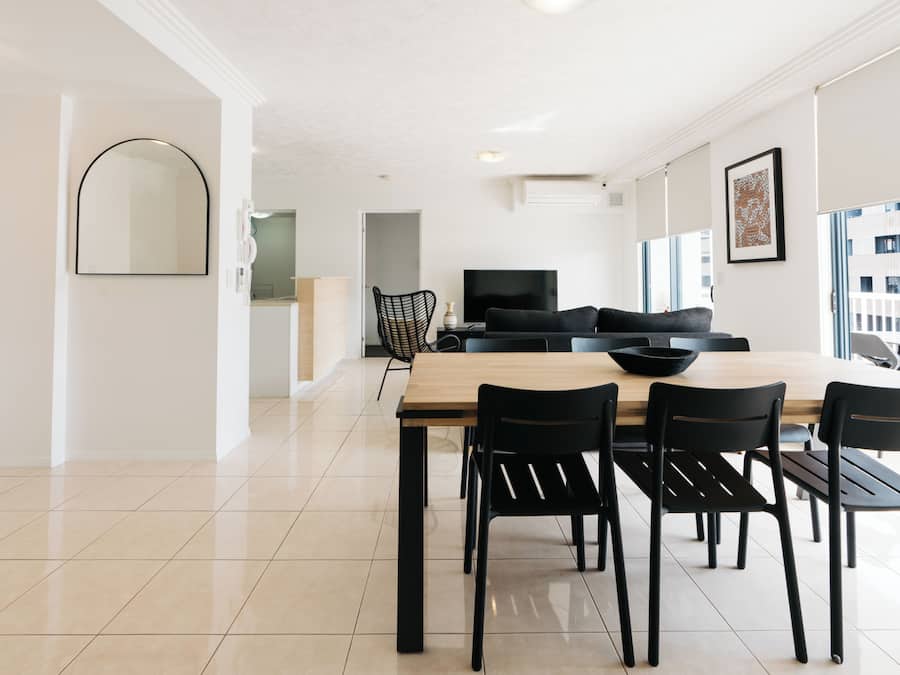 Uma área de jantar moderna com mesa de madeira e cadeiras pretas, um sofá preto e uma grande janela com vista para edifícios.