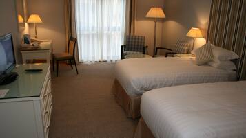 Quarto de hotel com duas camas, uma mesa com computador, uma cadeira e um abajur.