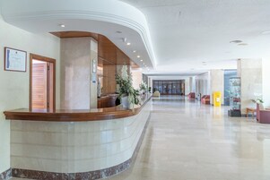 Uma área de recepção de hotel com um balcão curvo, uma porta de madeira e um certificado emoldurado na parede.
