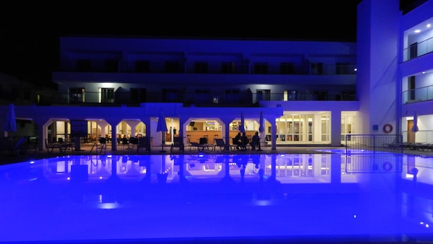 Piscina com borda iluminada em azul, um edifício com várias varandas e áreas de estar ao ar livre.
