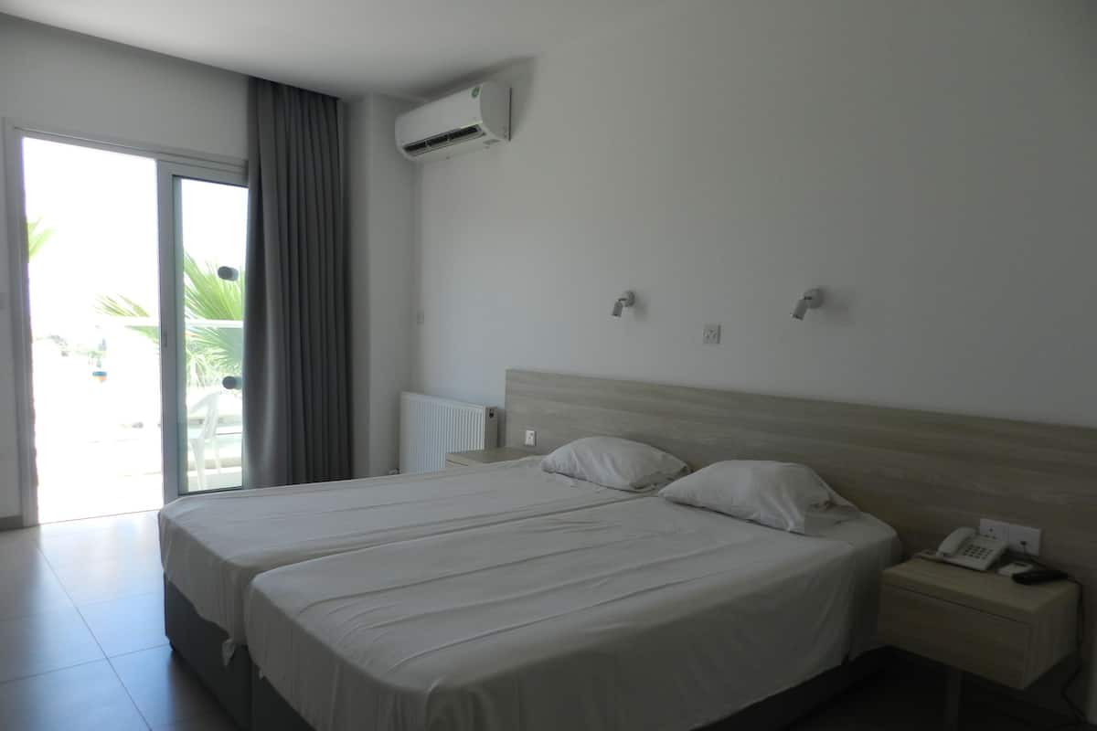 Quarto de hotel com duas camas, uma mesa de cabeceira com telefone e um aparelho de ar condicionado na parede.
