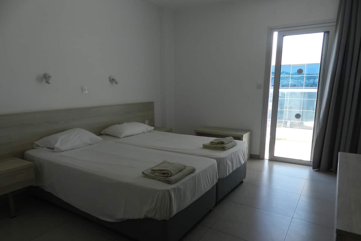 Quarto de hotel com duas camas, uma mesinha e vista da cidade por uma grande janela.