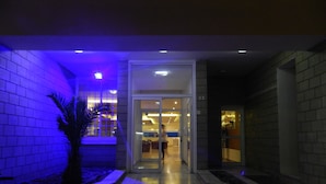 Entrada de hotel com porta de vidro, degraus de acesso e uma palmeira à esquerda.